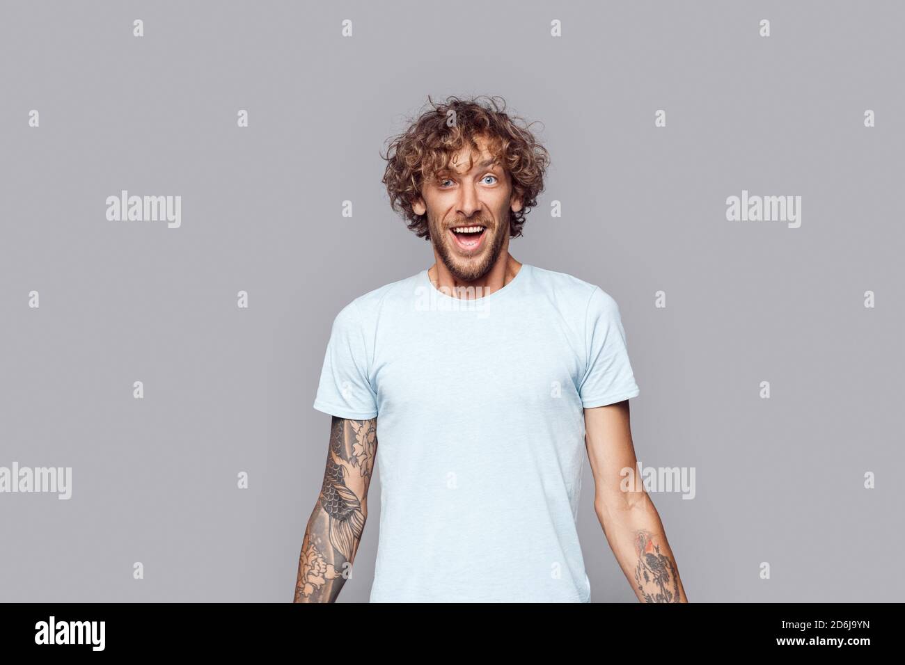 Freestyle. Man with curly hair standing isolated on grey smiling ...
