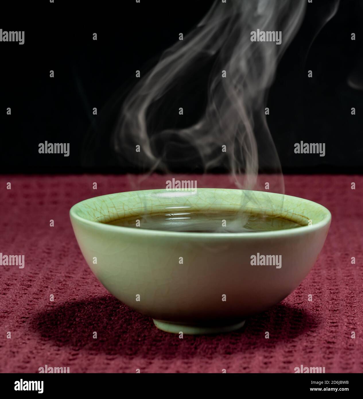 Chinese tea steaming in a small green teacup isolated with a black ...