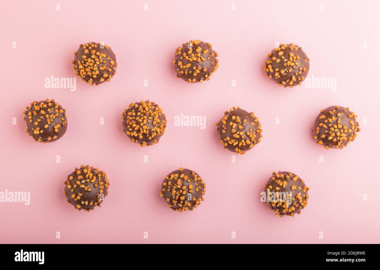 Chocolate caramel ball candies with almonds in a row on a pastel pink ...