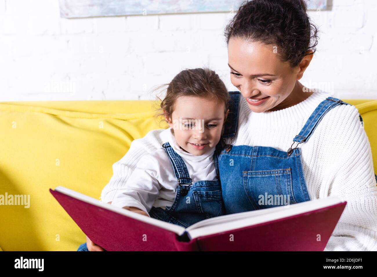 Mother embracing daughter reading book at home Stock Photo - Alamy