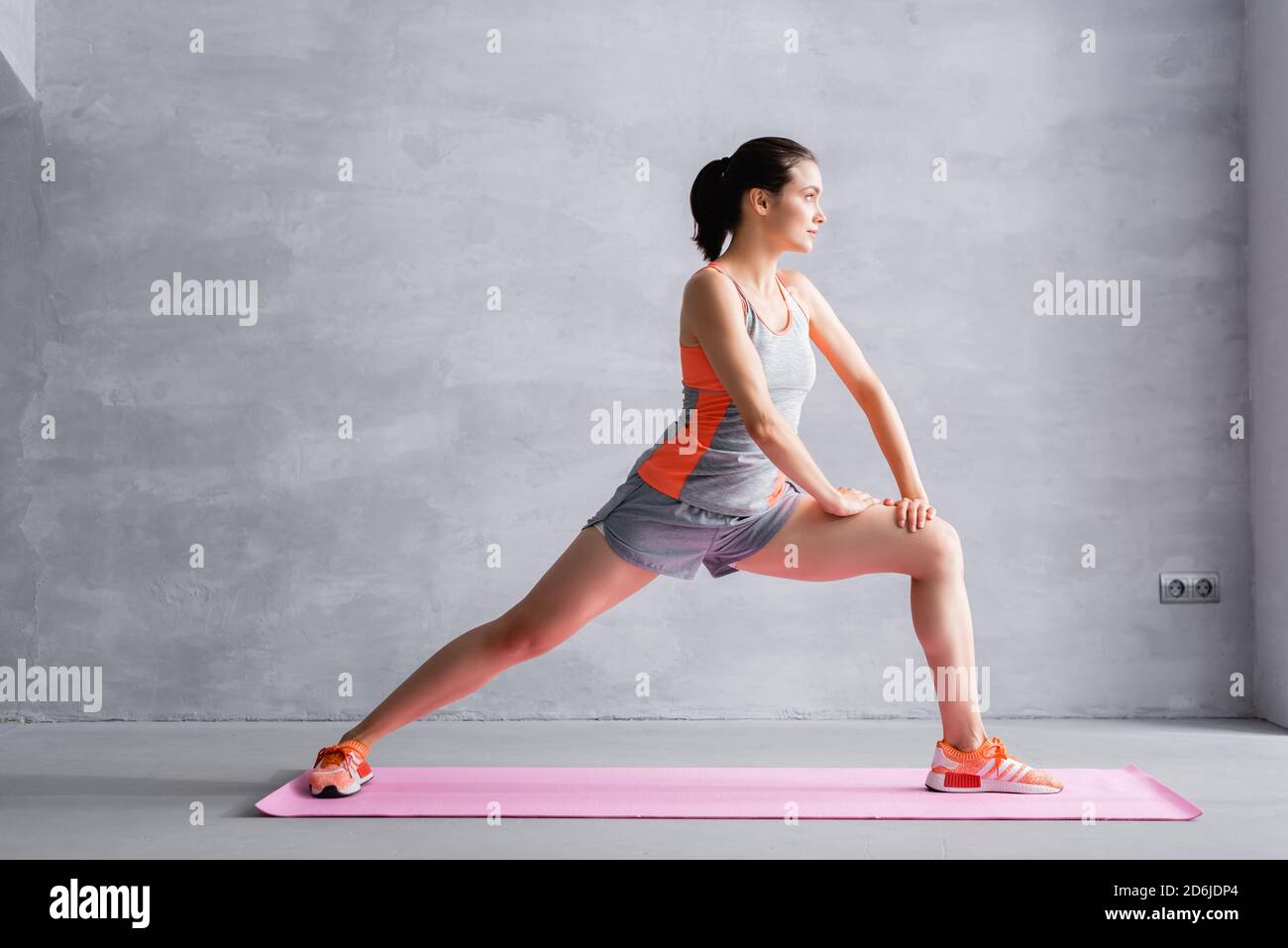 Side view of sportswoman looking away and doing lunge on fitness mat ...