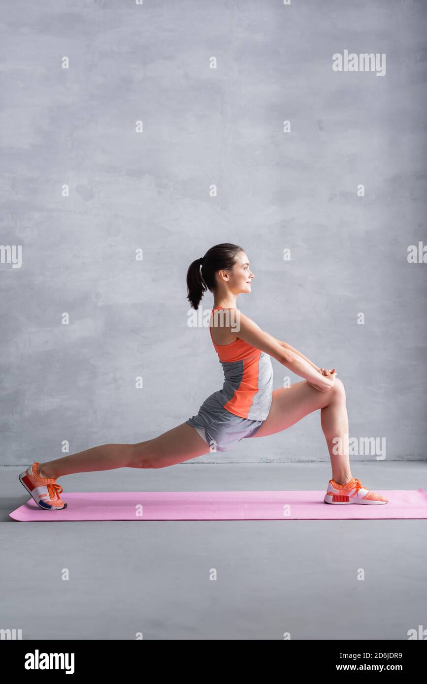 Side view of sportswoman doing lunge on fitness mat on grey background ...