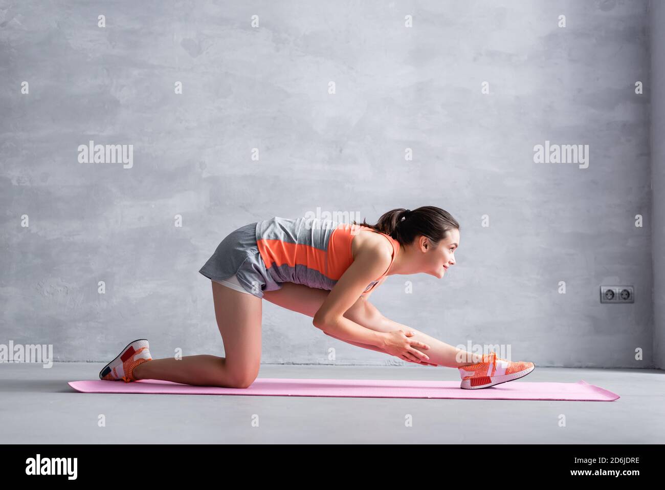 Side view of sportswoman doing lunge and stretching leg on fitness mat ...