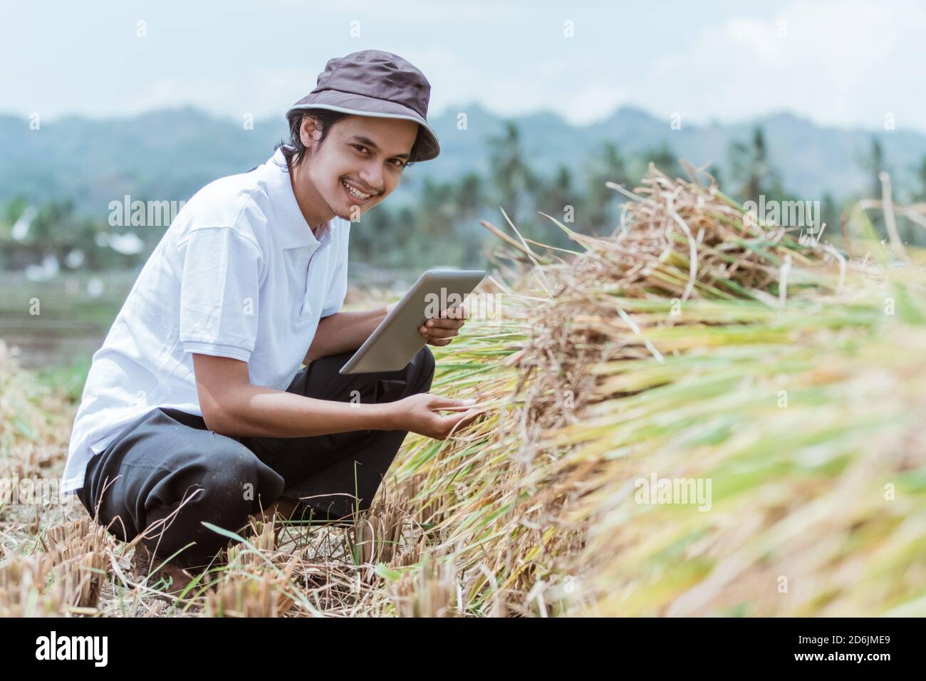 a rice seller in the rice fields smiles while holding a tablet while ...