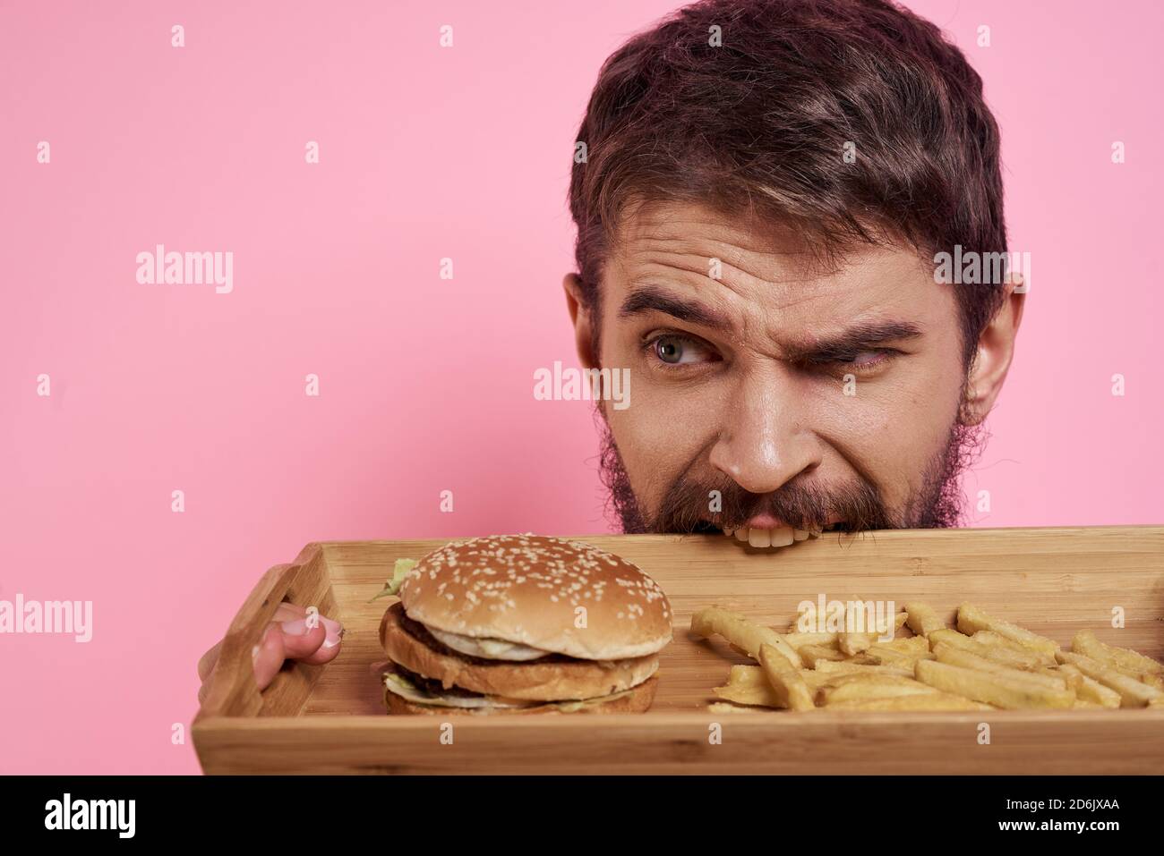 Aggressive guy with a tray in his hands hamburger fries pink background ...