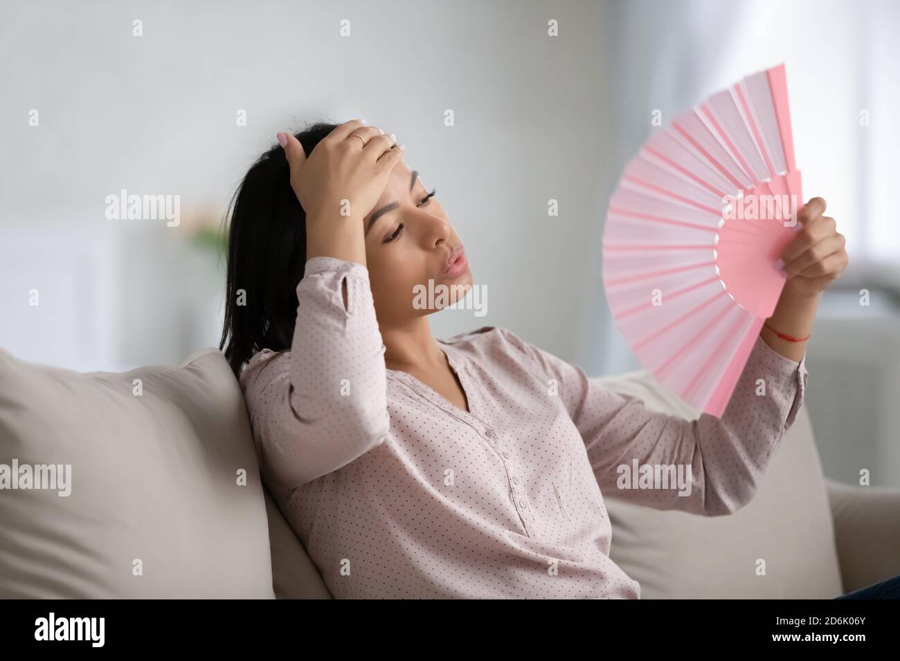 Overheated biracial woman use hand fan at home Stock Photo - Alamy