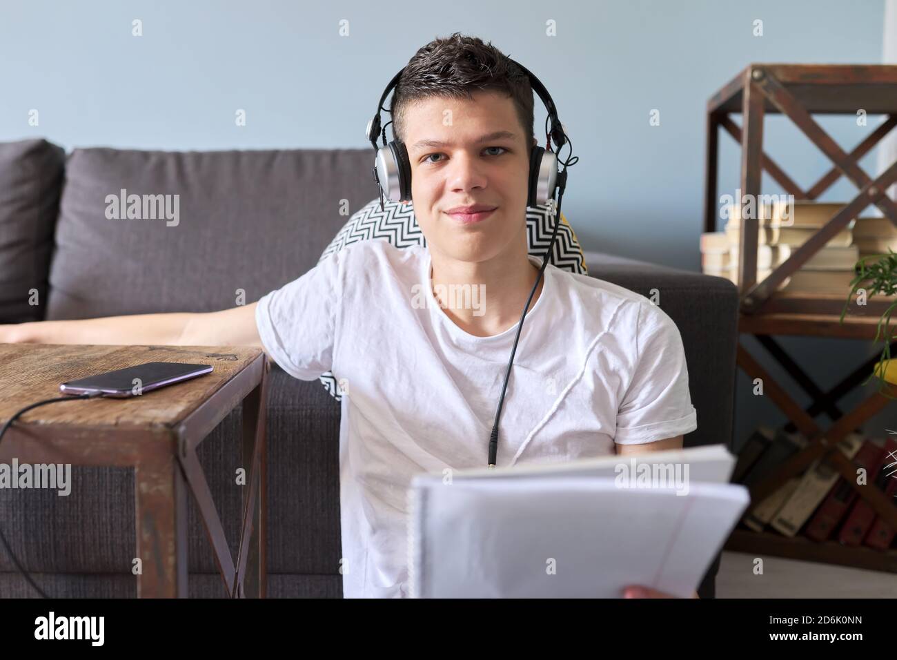Teenager student in headphones with notebook and smartphone studying ...