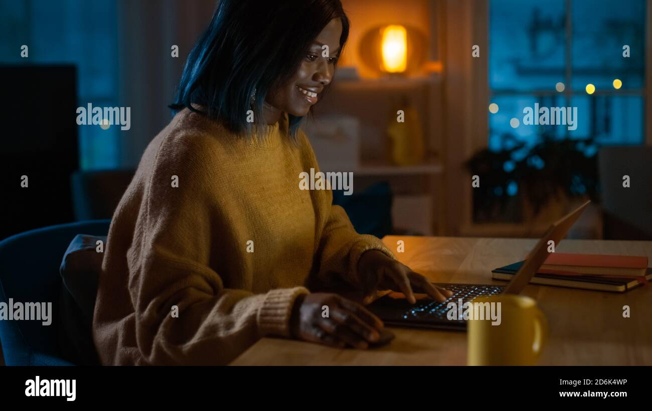 Portrait of Beautiful Black Girl Uses Computer while Sitting at Her Desk at Home, She's Wearing ...