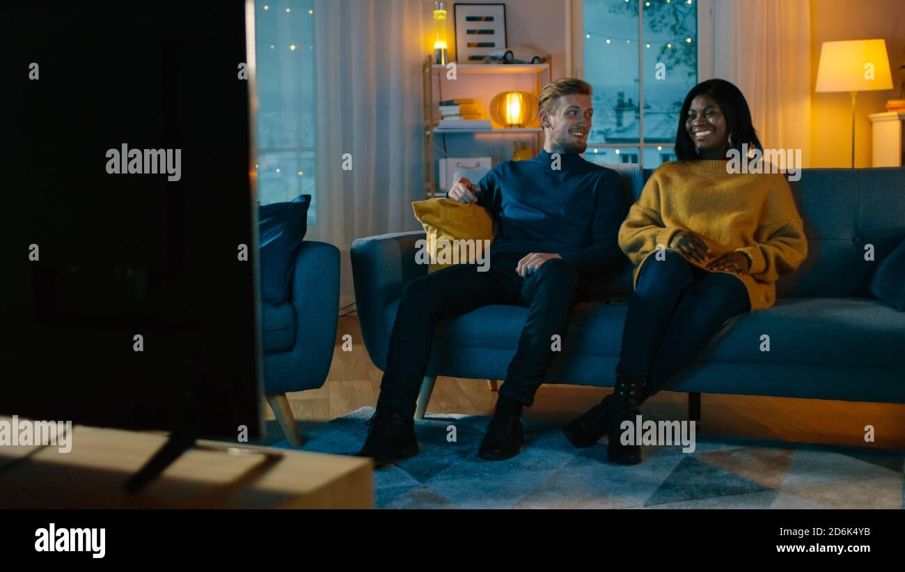 Happy Diverse Young Couple Watching Comedy on TV while Sitting on a ...