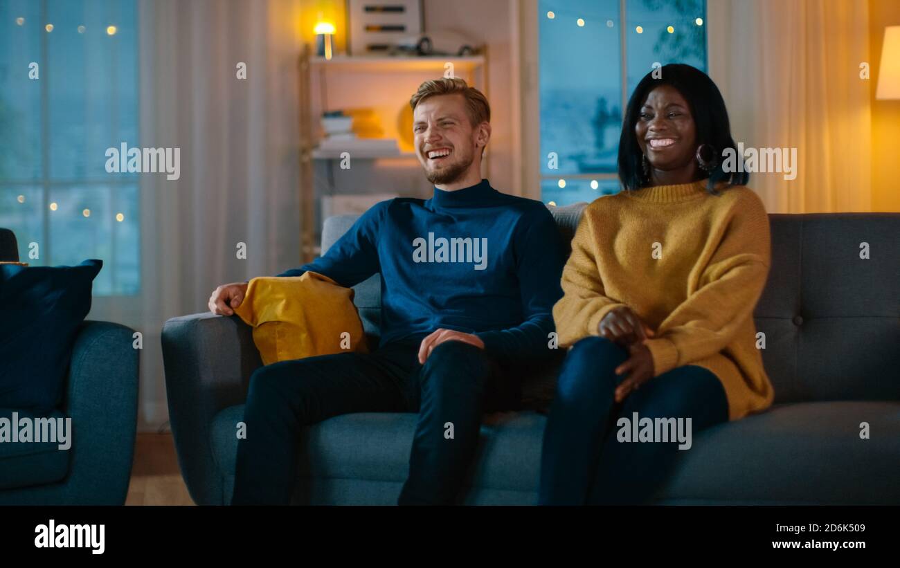 Happy Diverse Young Couple Watching Comedy on TV while Sitting on a ...