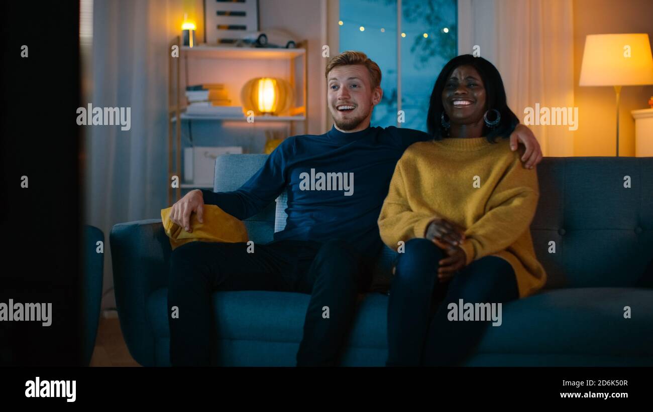 Happy Diverse Young Couple Watching Comedy on TV while Sitting on a ...