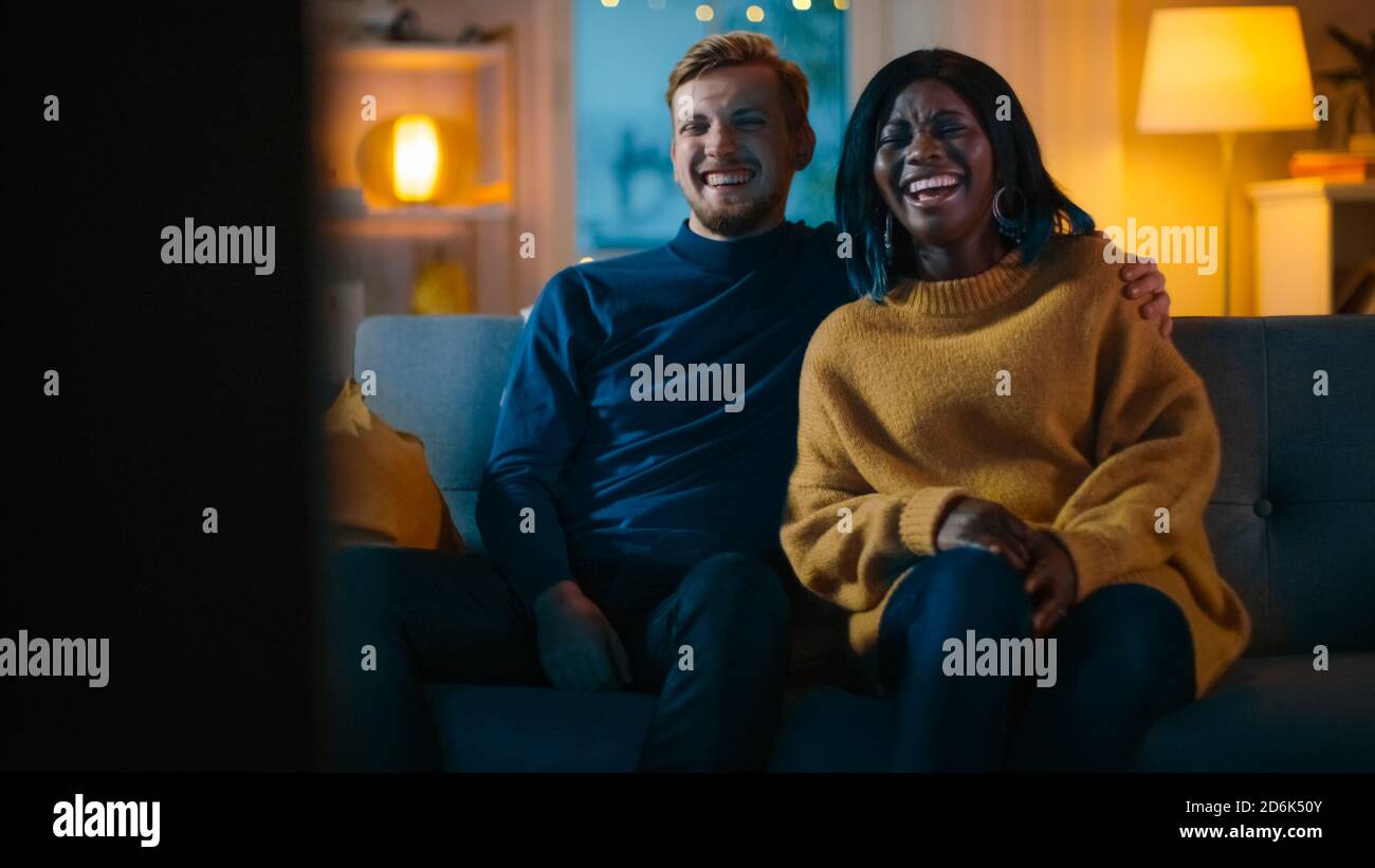Happy Diverse Young Couple Watching Comedy on TV while Sitting on a ...