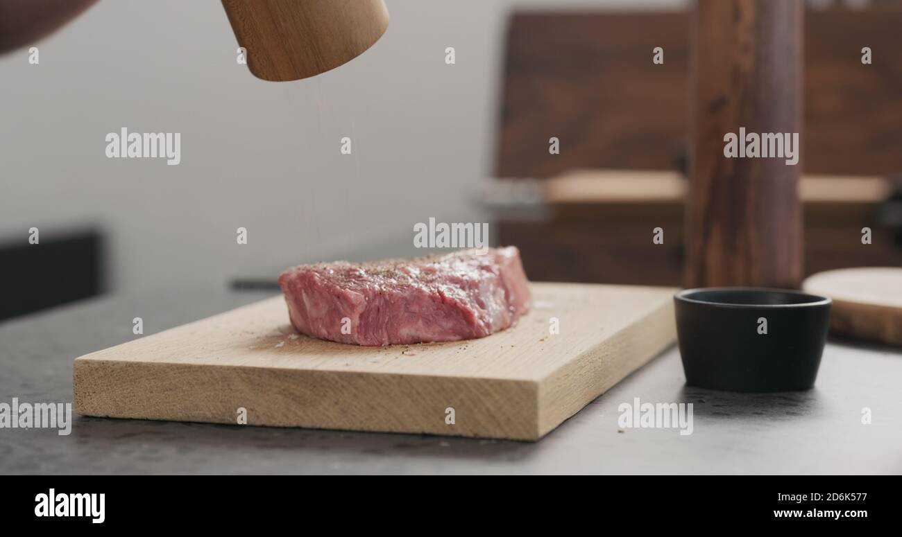 Man seasoning raw ribeye steak on oak wood board, wide photo Stock ...
