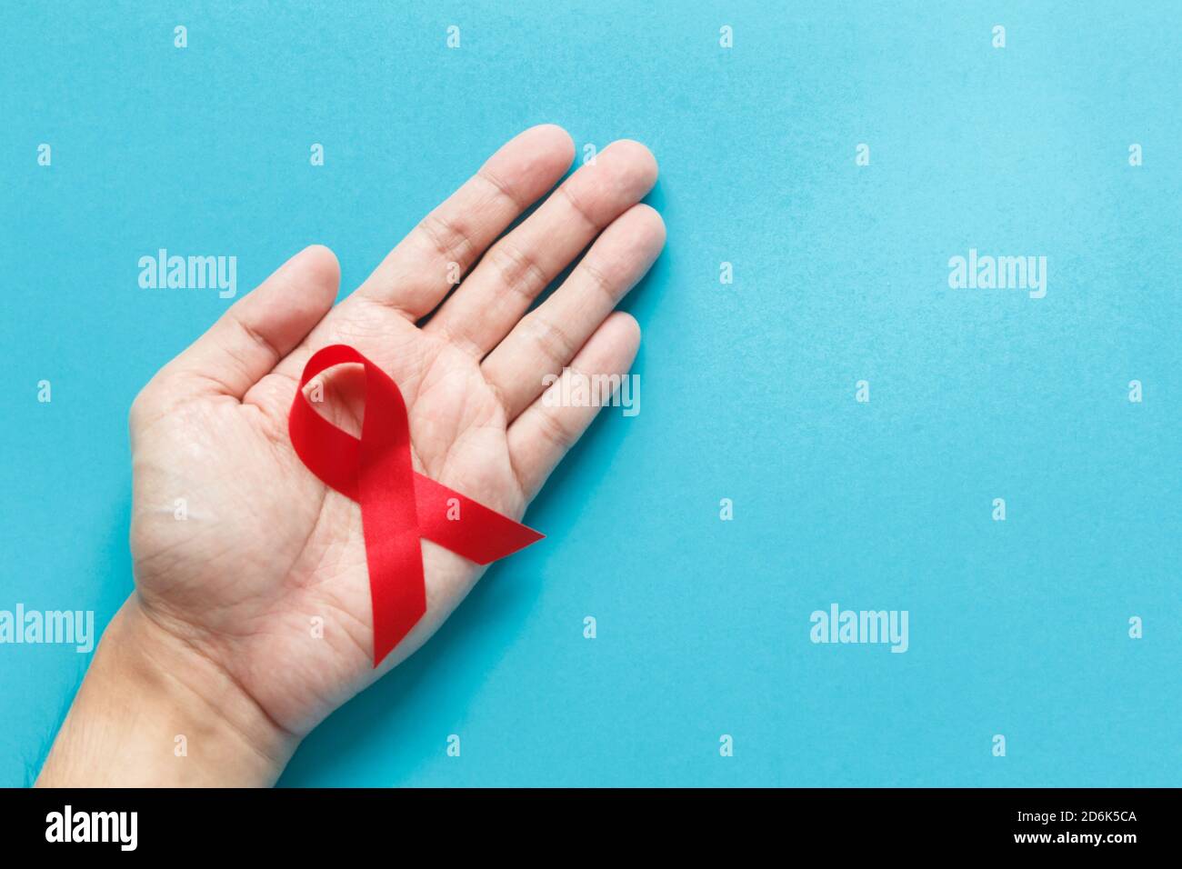 red AIDS awareness ribbon on the hand with blue paper background. World ...