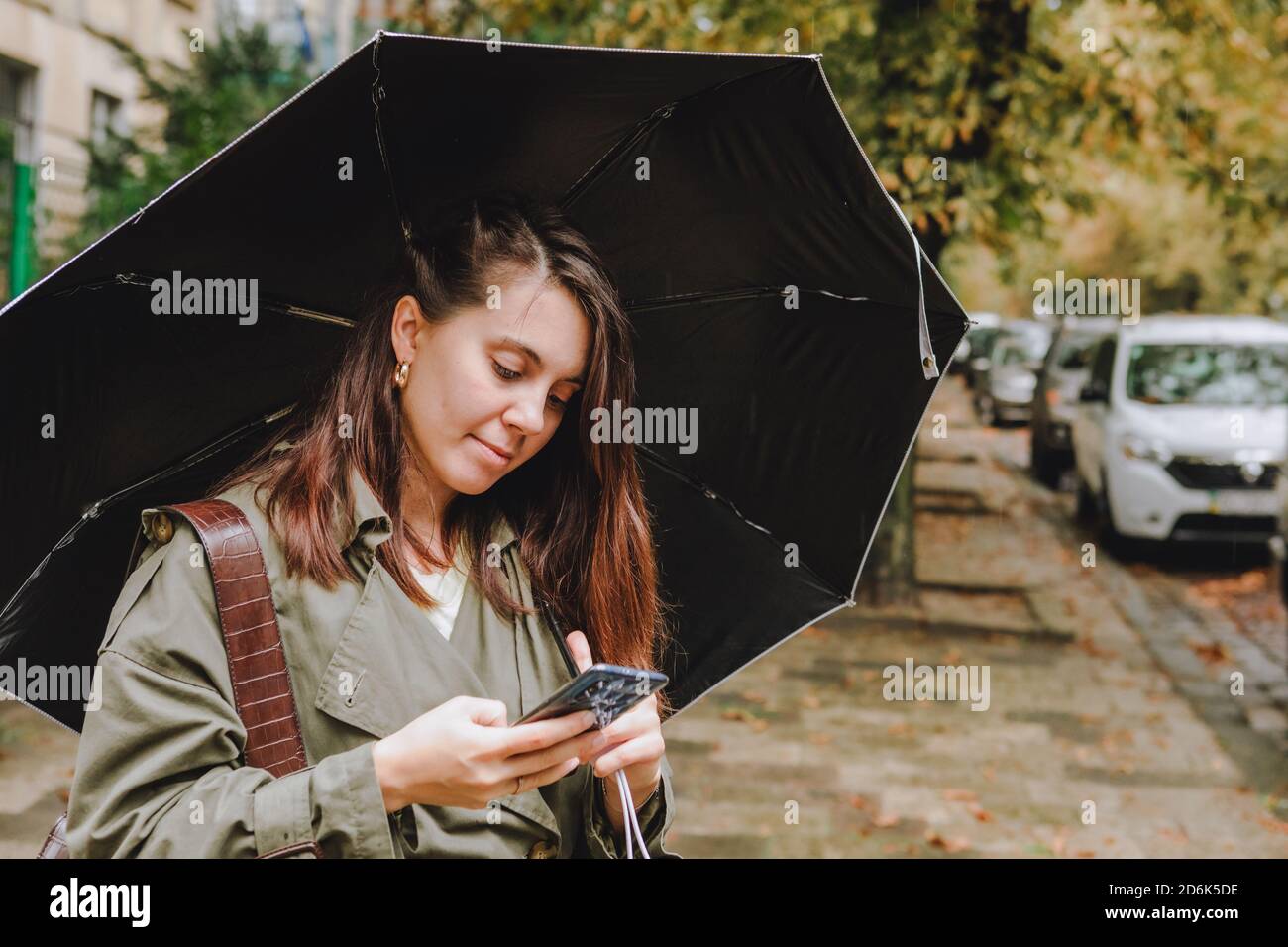 young pretty woman talking on the phone at city street hiding from rain ...