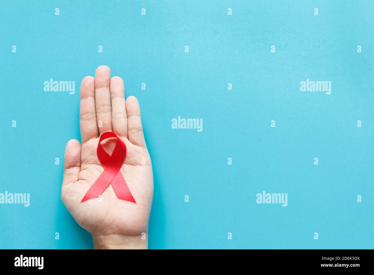 red AIDS awareness ribbon on the hand with blue paper background. World ...