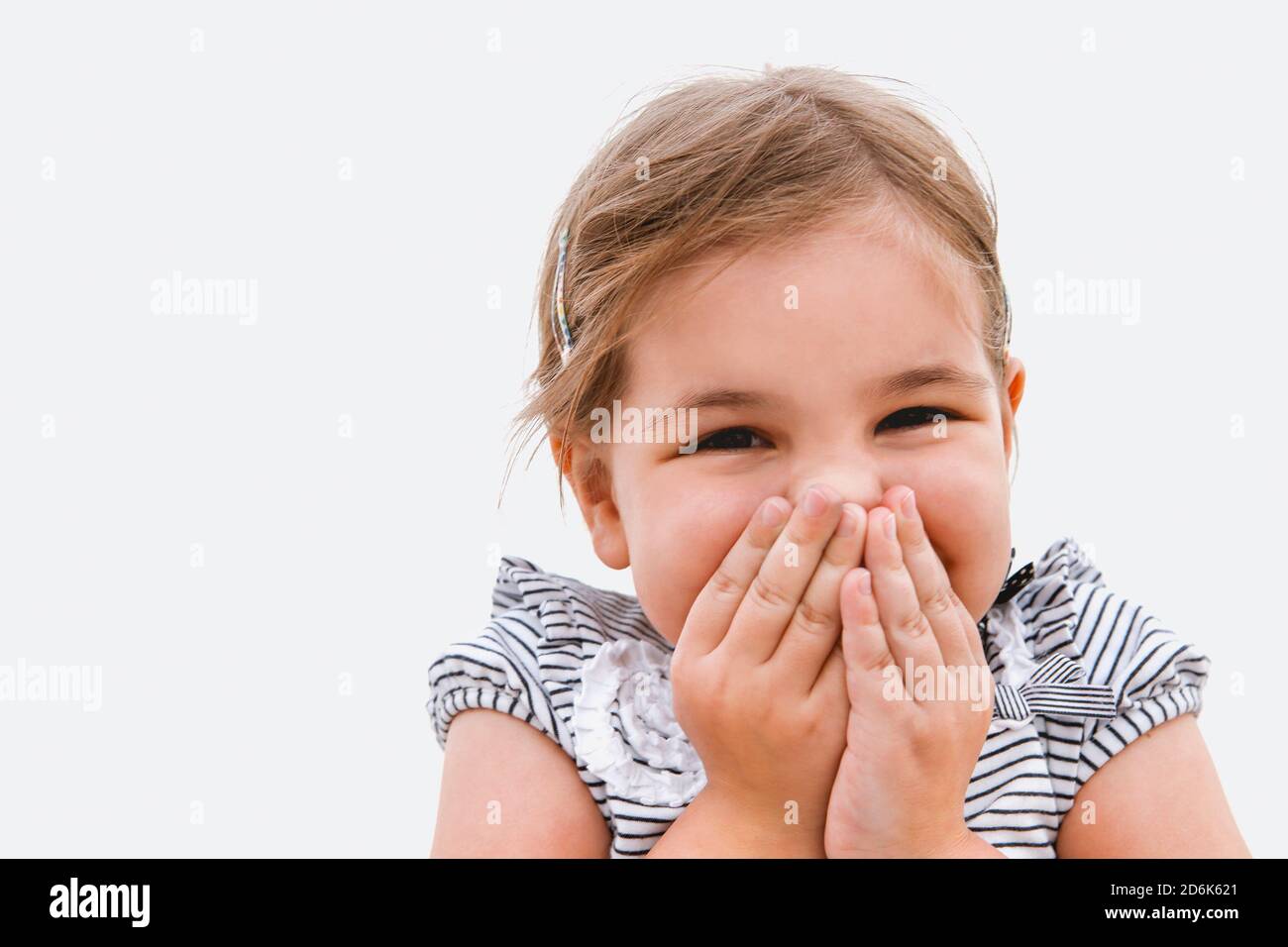 Delighted child looking at camera while laughing and covering mouth ...