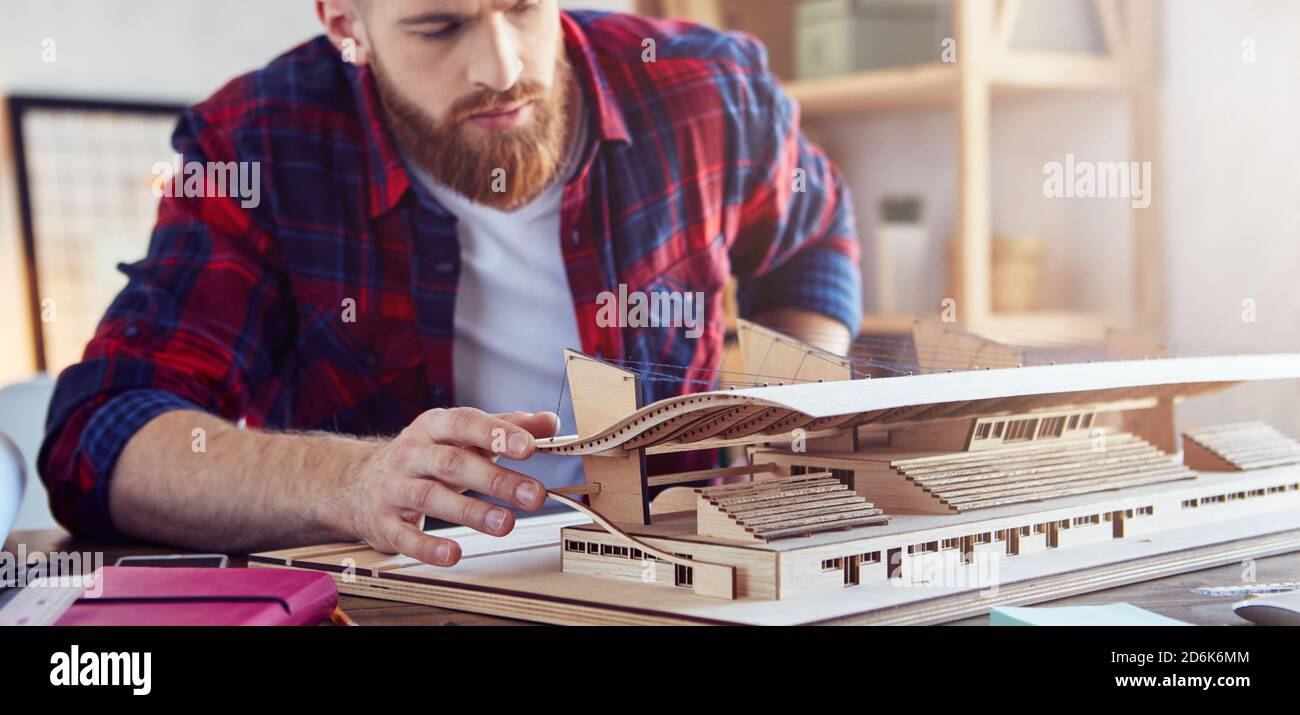 Cropped photo of young creative designer in office looking at model of ...