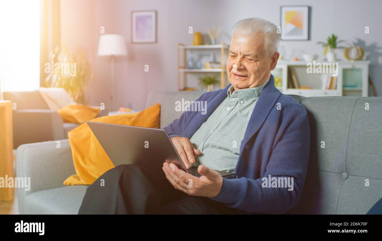 Progressive Senior Man at Home Sitting on Sofa Uses Laptop Computer ...
