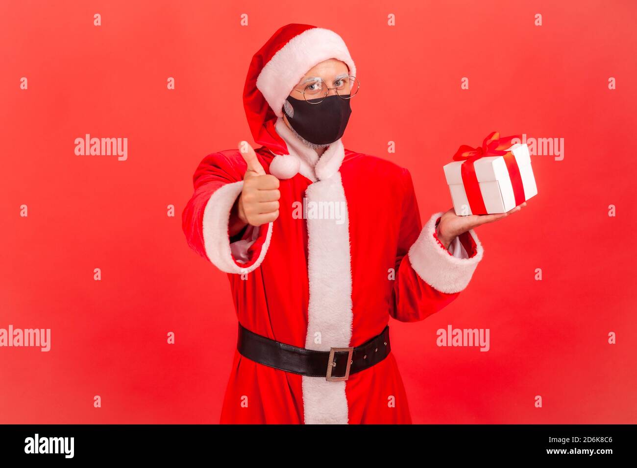 Satisfied santa claus in protective mask on face holding gift box with ...