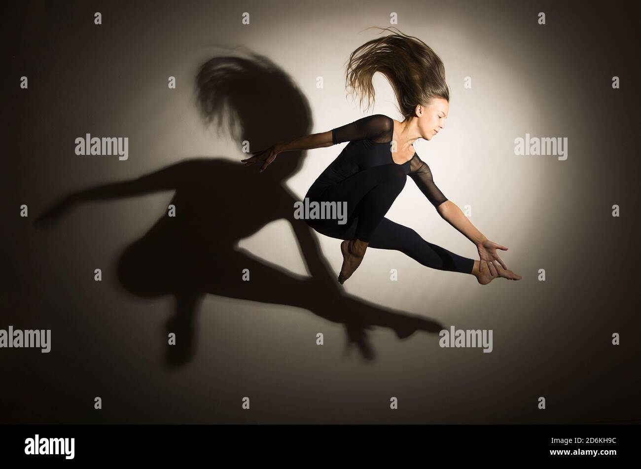 woman in dark performs gymnastic jumping, on a white background there ...