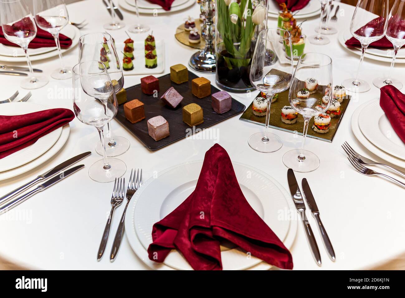 Round table with white tablecloth and red napkins, set of cutlery with ...