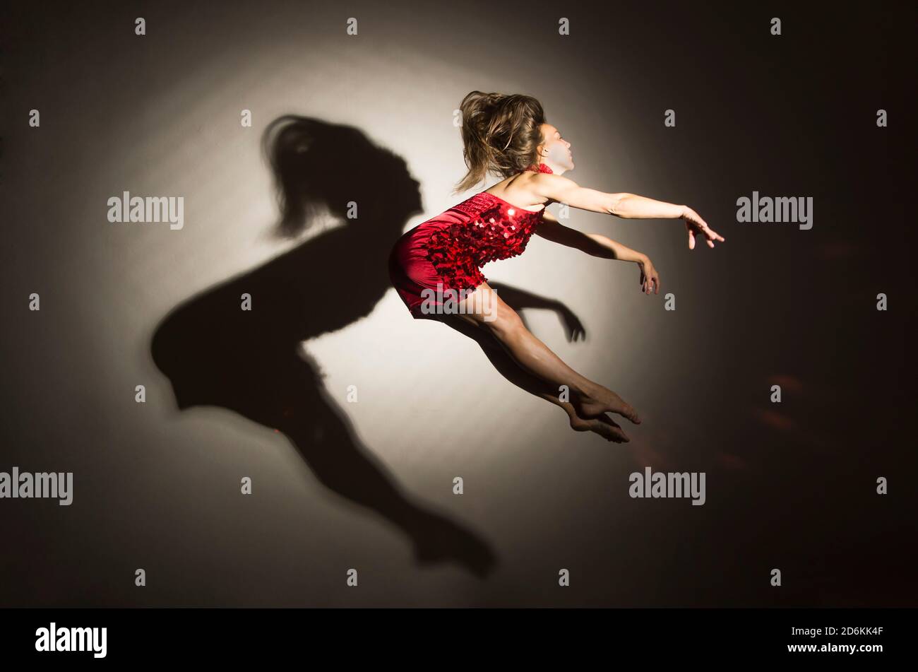 A woman in a red dress performs gymnastic jumps, a shadow from a figure ...