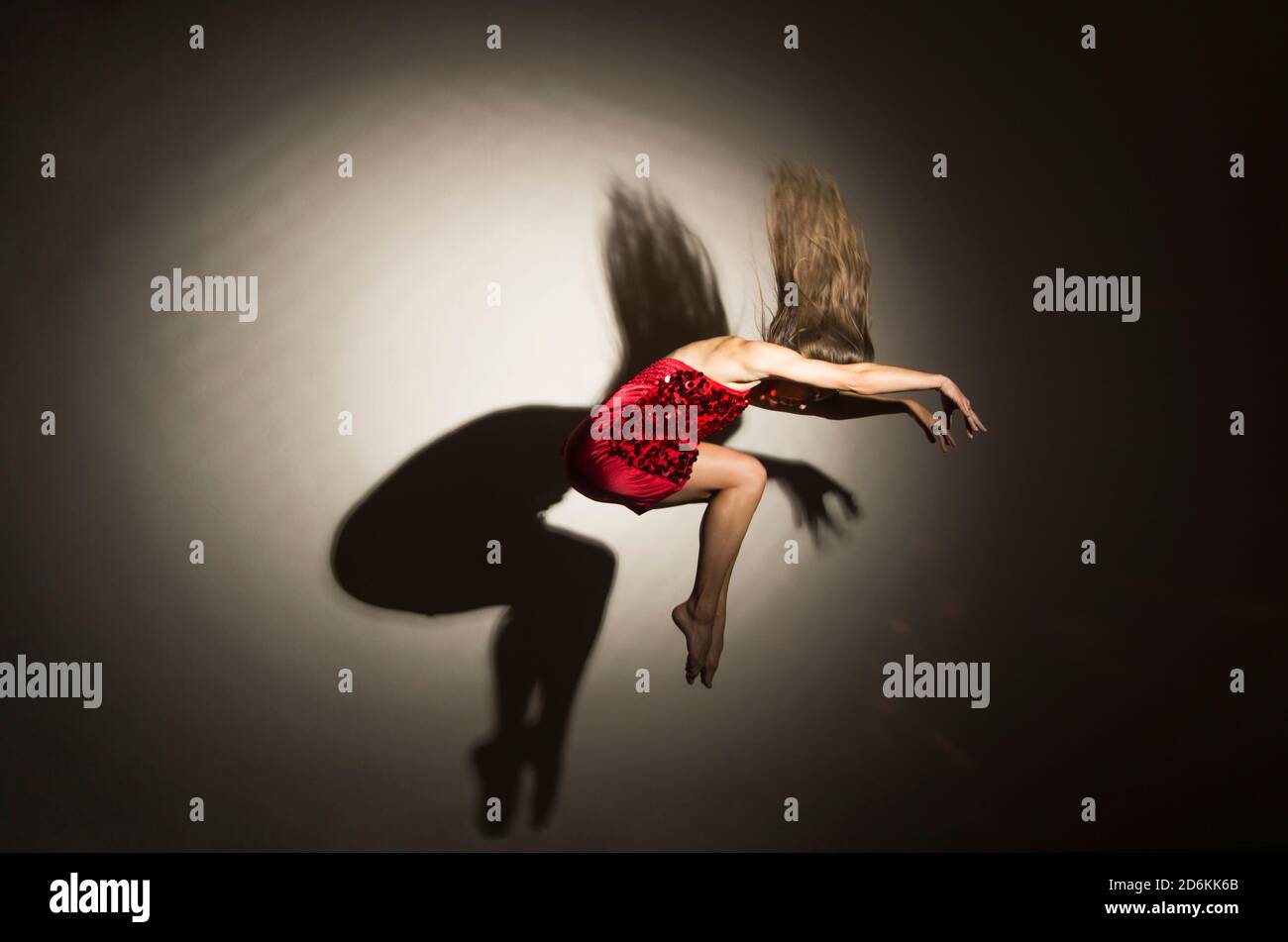 A woman in a red dress performs gymnastic jumps, a shadow from a figure ...