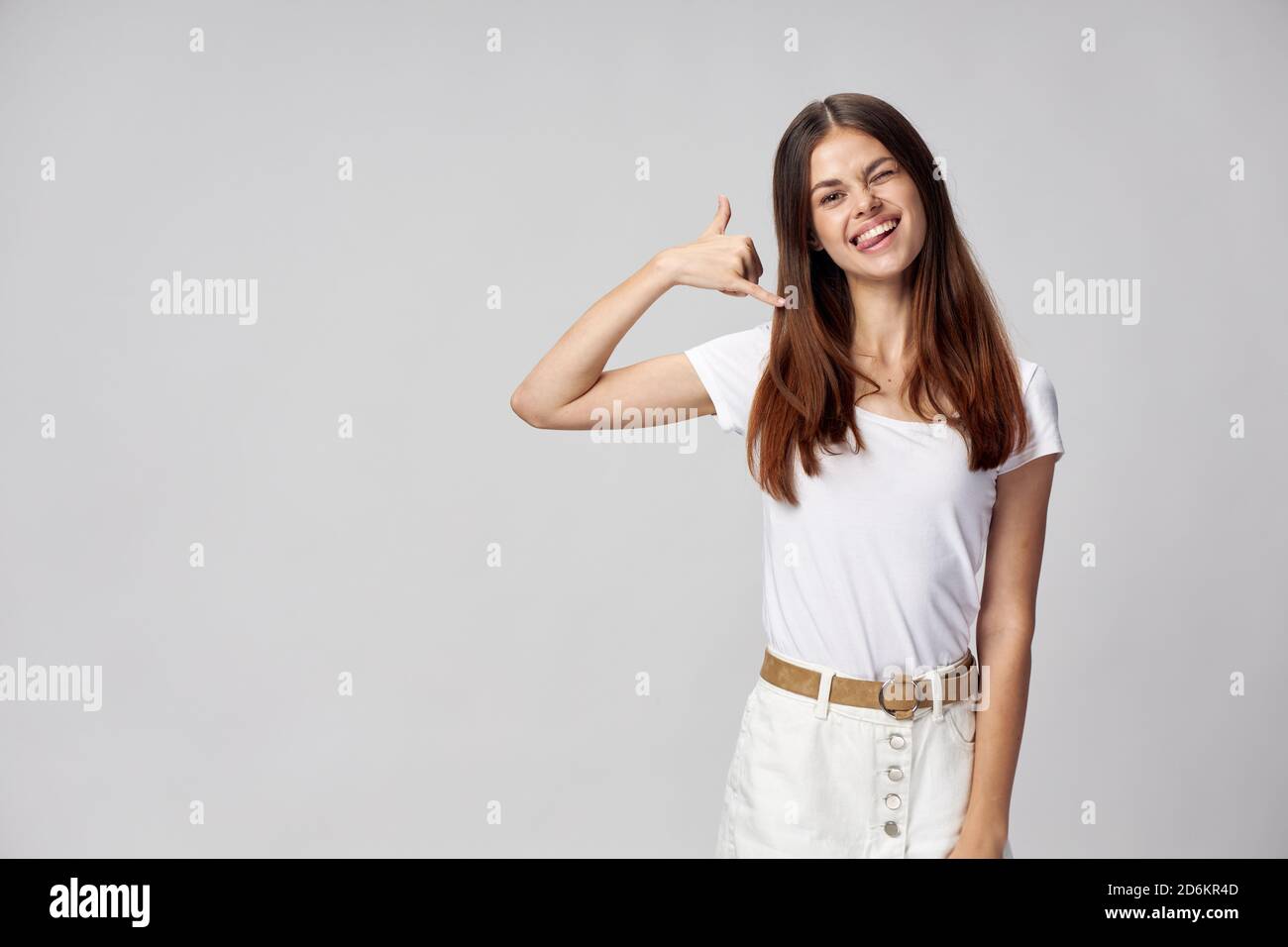 A woman holds two fingers near her face and winks on a light background ...