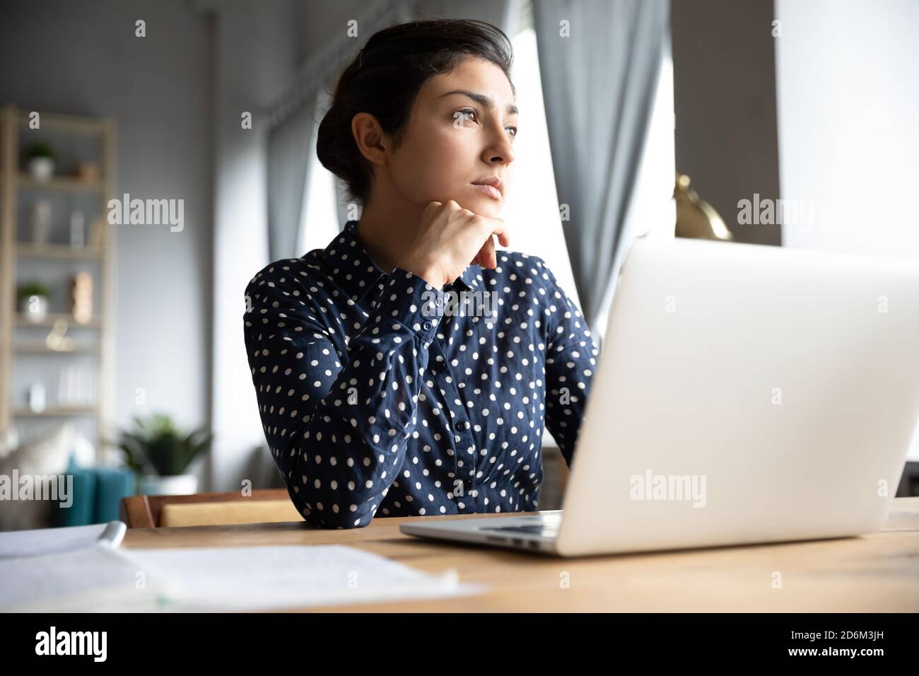 Thoughtful Indian female distracted from computer work looking into ...
