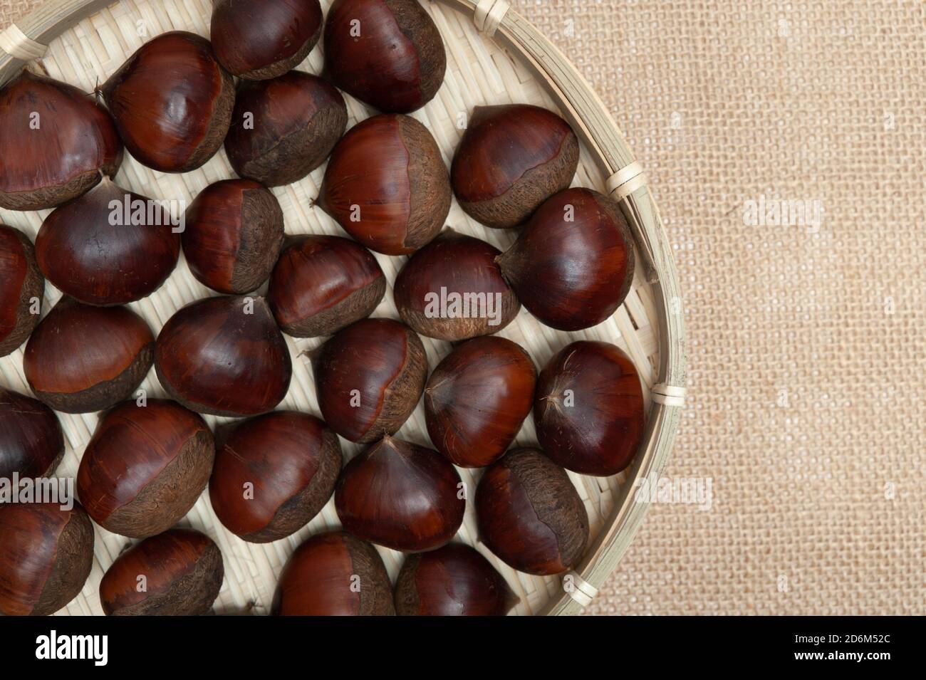 Chestnuts in bamboo basket isolated on jute background. Close-up. Copy ...