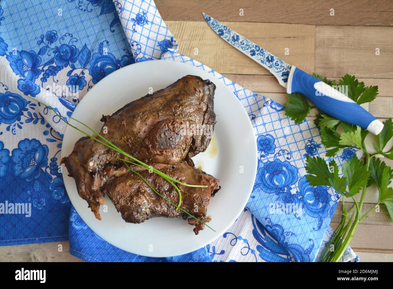Roasted hare legs on rustic wooden surface with blue and white ...