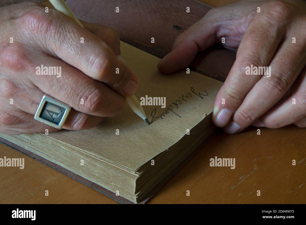 Middle aged male wearing a ring, writing in a notebook using a pencil ...