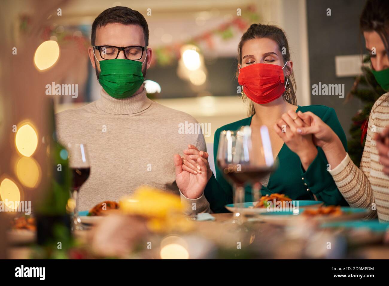 Group of friends in masks praying over Christmas Thanksgiving table at ...