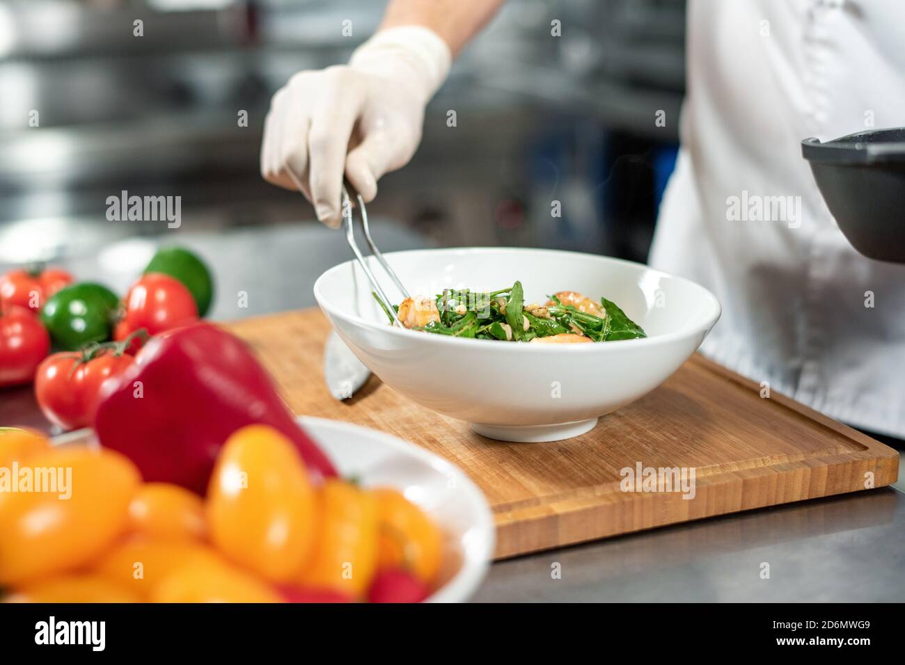 Gloved hand of young chef with fork putting cooked meal into white ...