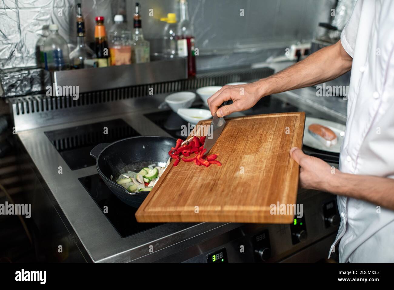 Hands of young chef in white uniform putting chopped capsicum into ...