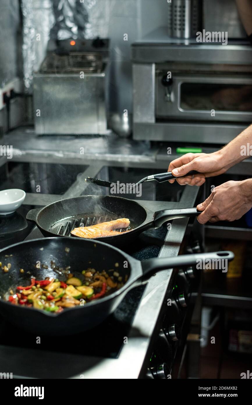 Hands of male chef roasting piece of salmon while cooking fish and ...