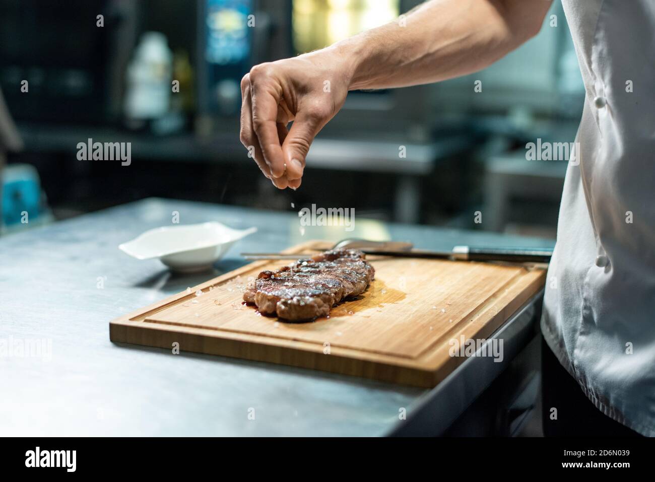 Hand of chef sprinkling spices on roasted beef steak during preparation ...