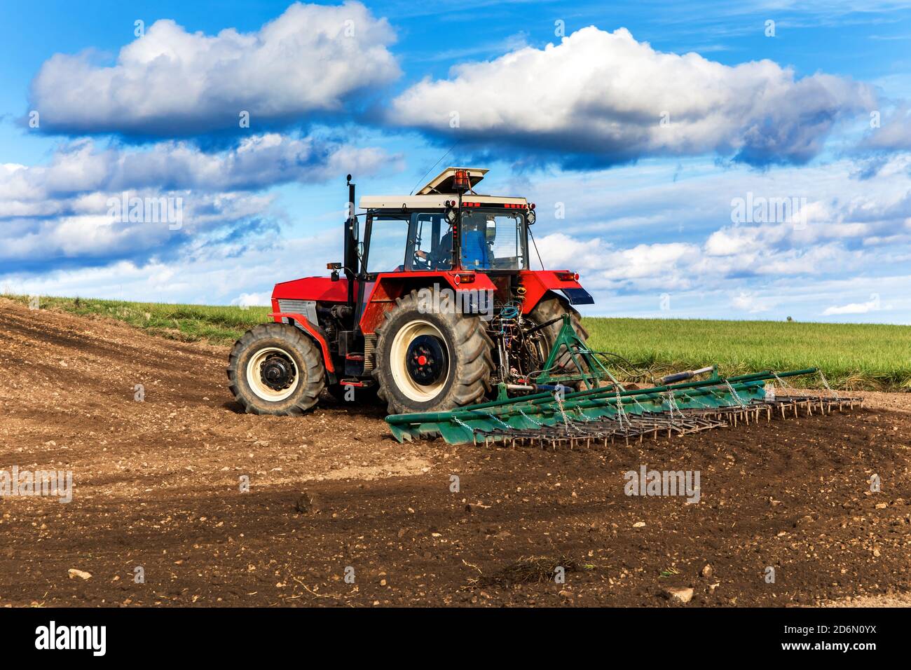 Agriculture red tractor cultivating field over blue sky. Old red ...