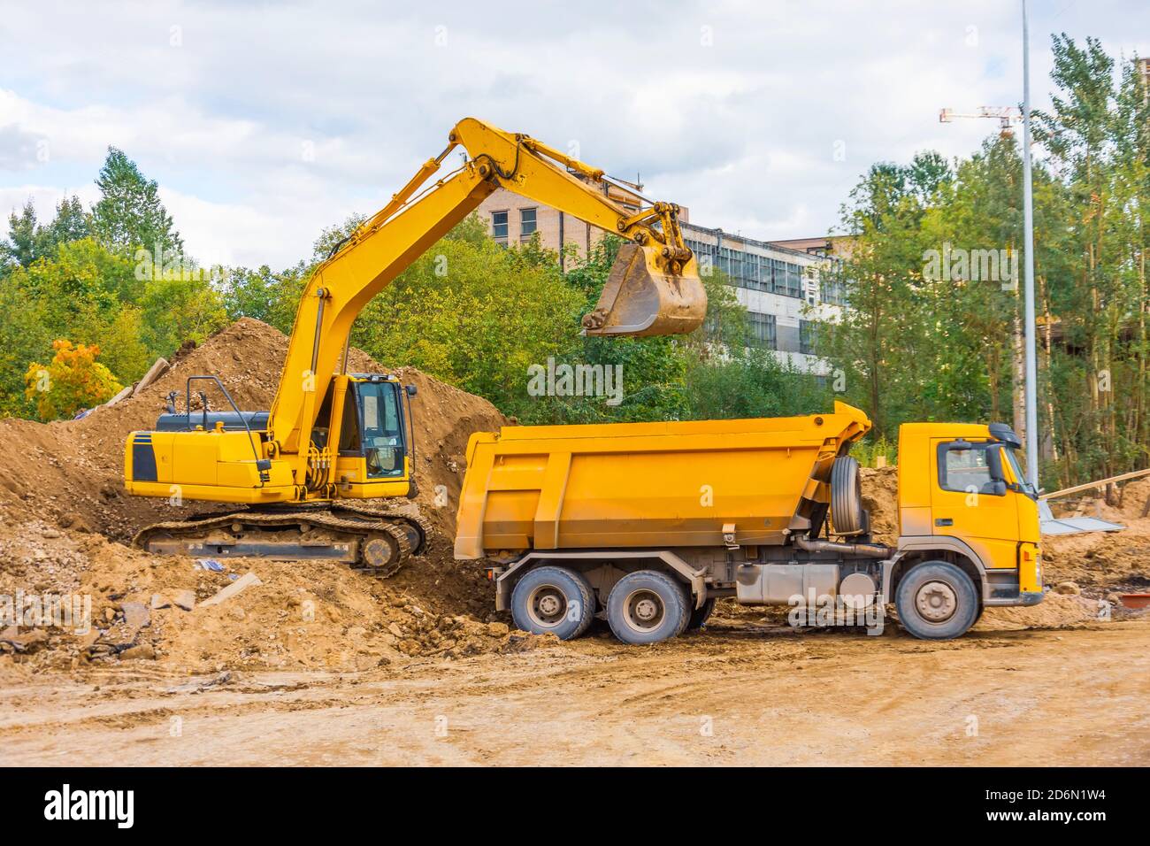 Yellow truck and excavator load soil with sand during road construction ...