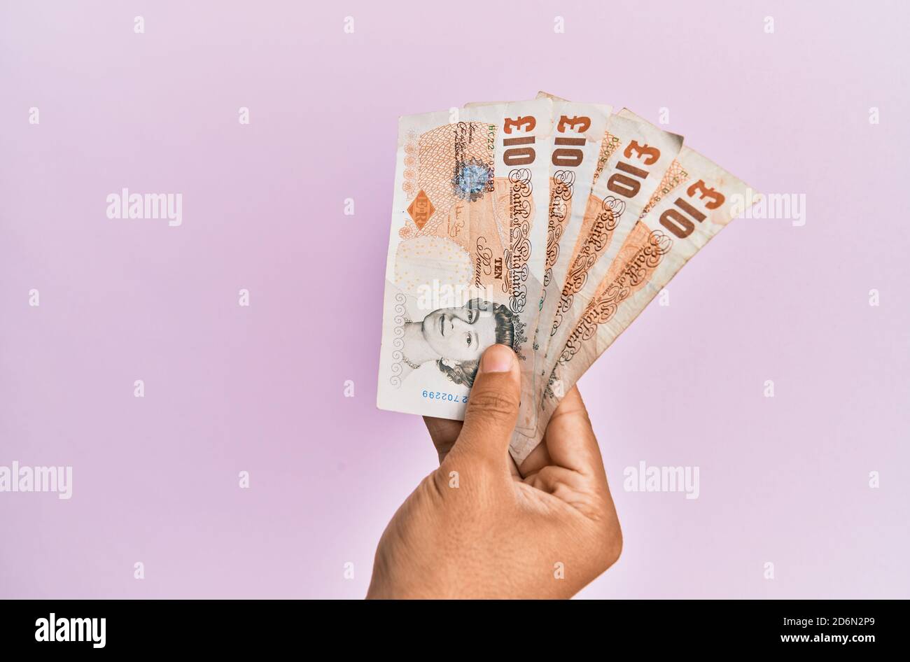 Hispanic hand holding 10 uk pounds banknotes over isolated pink ...