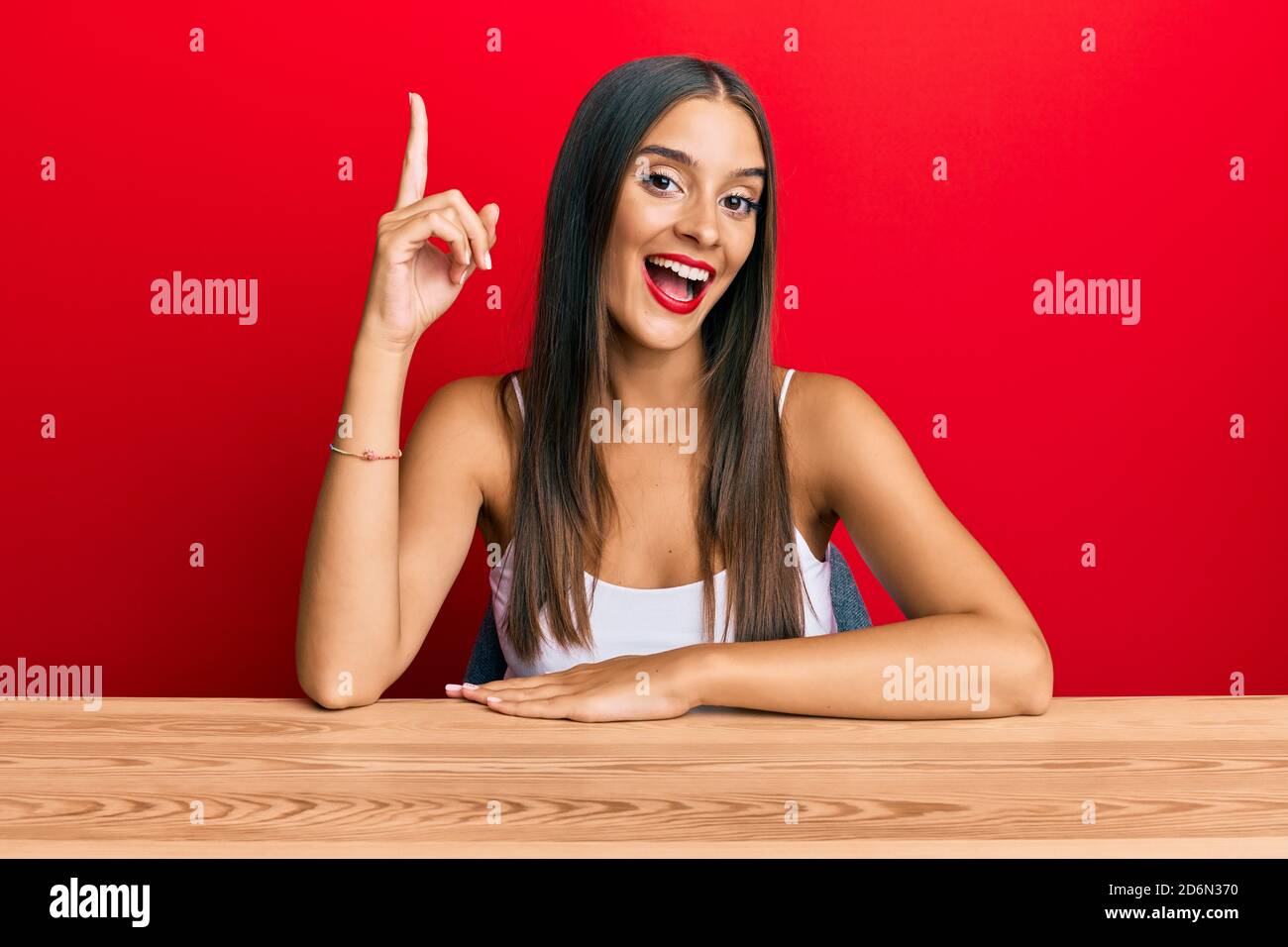 Young hispanic woman wearing casual clothes sitting on the table ...