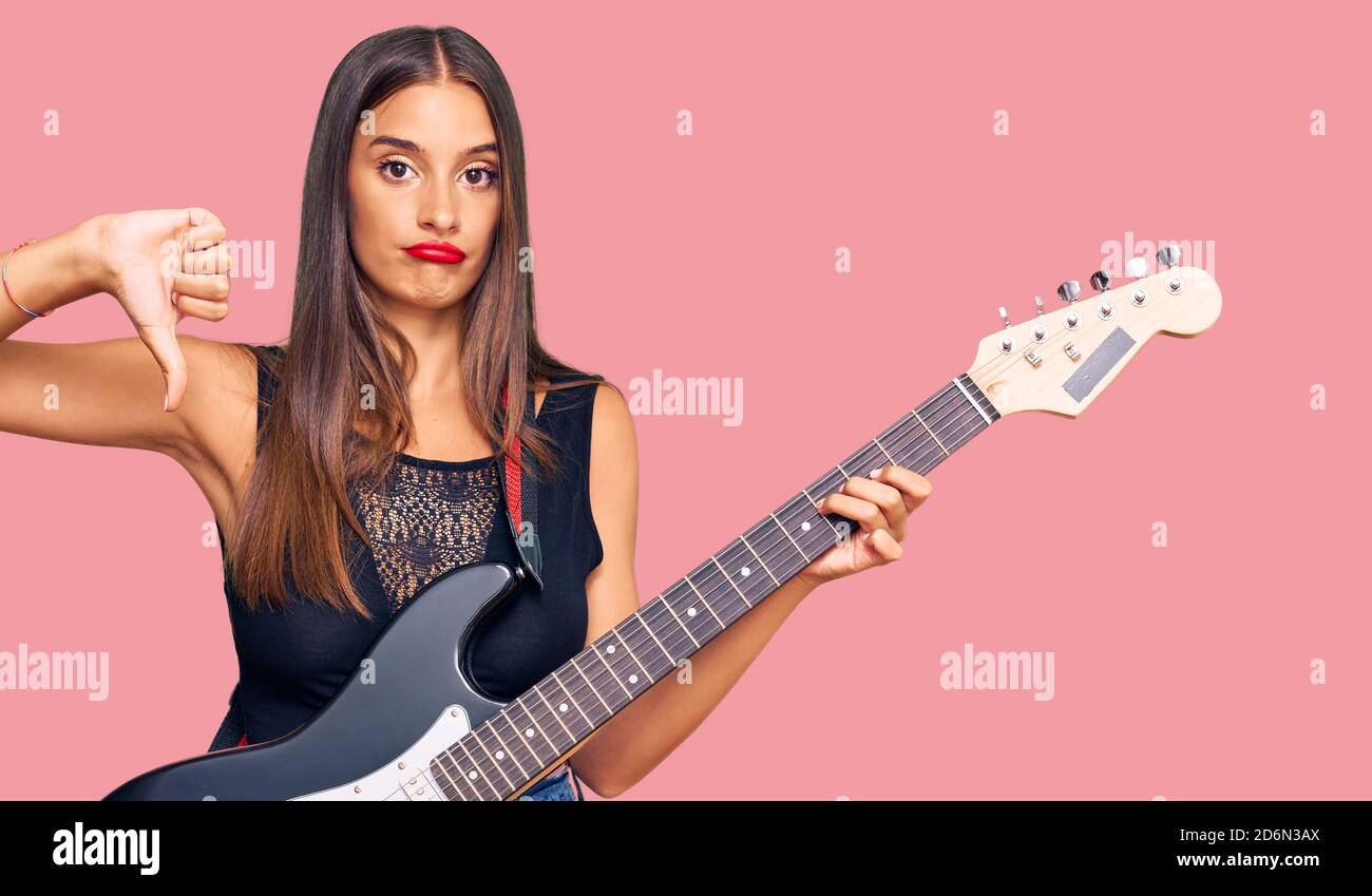 Young hispanic woman playing electric guitar with angry face, negative ...