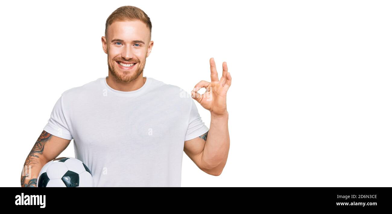 Young irish man holding soccer ball doing ok sign with fingers, smiling ...