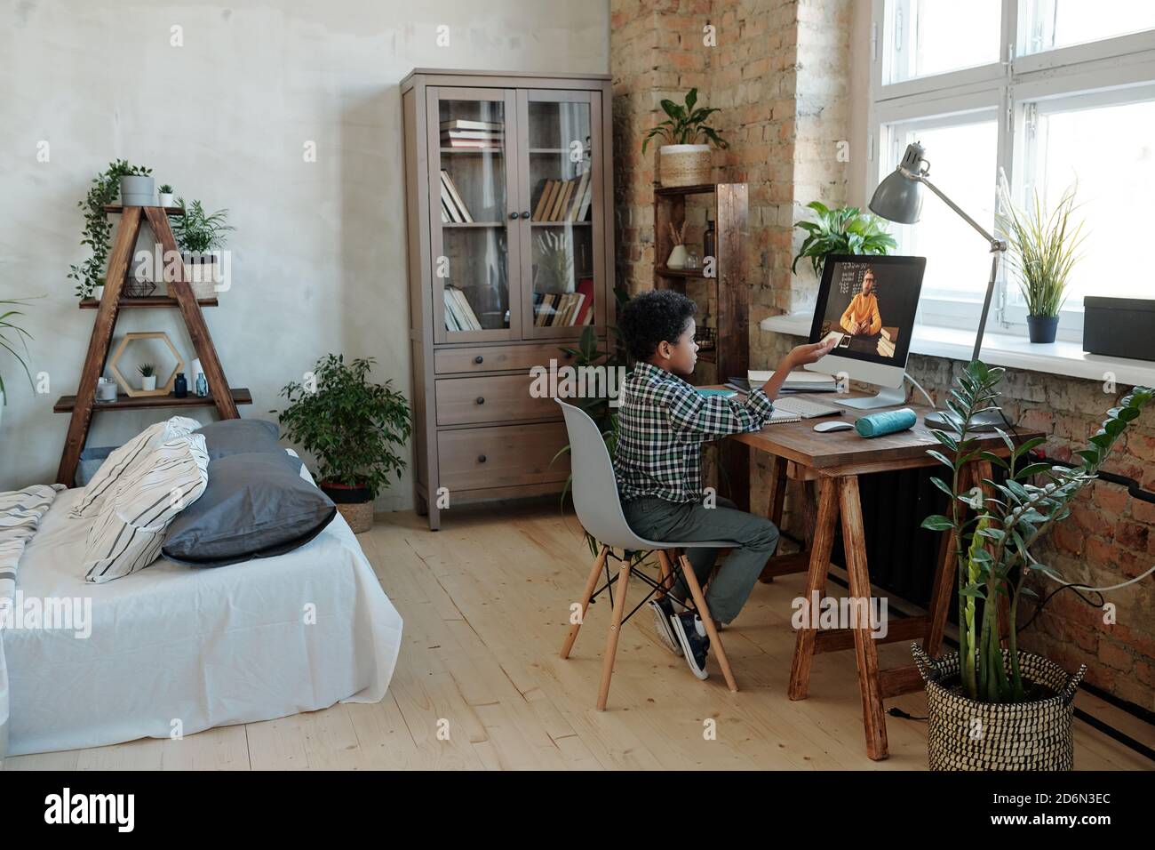 Contemporary little schoolboy sitting by table in front of computer ...