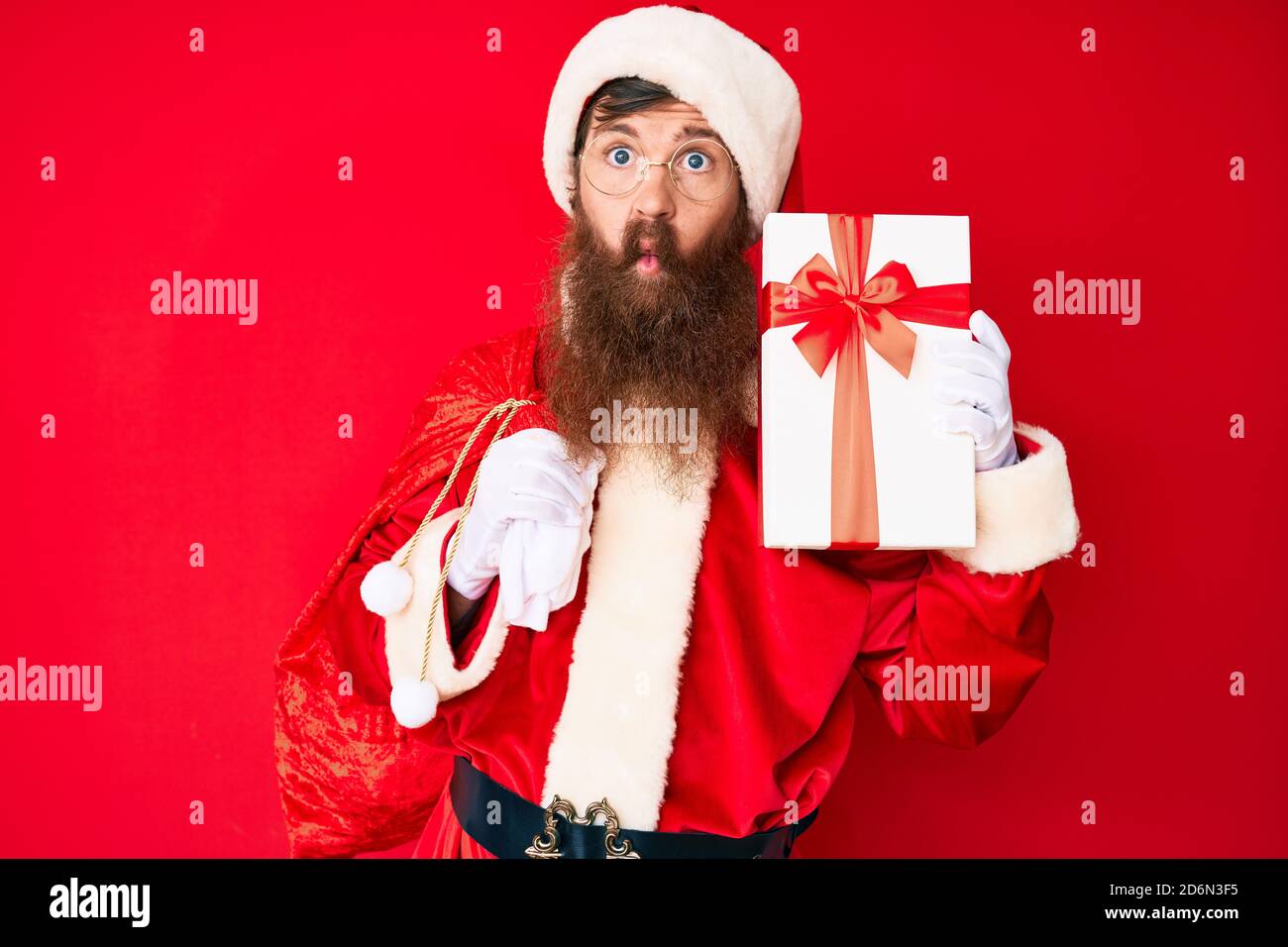 Handsome young red head man with long beard wearing santa claus costume ...