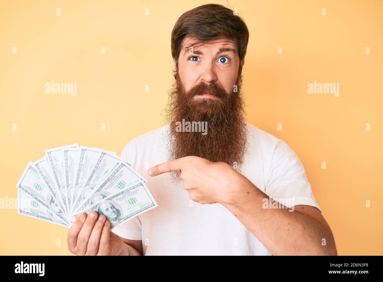 Handsome young red head man with long beard holding dollars skeptic and ...