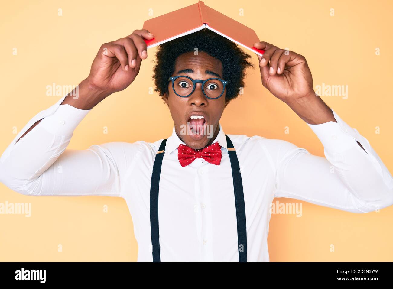 Handsome african american nerd man with afro hair holding book over head celebrating crazy and ...