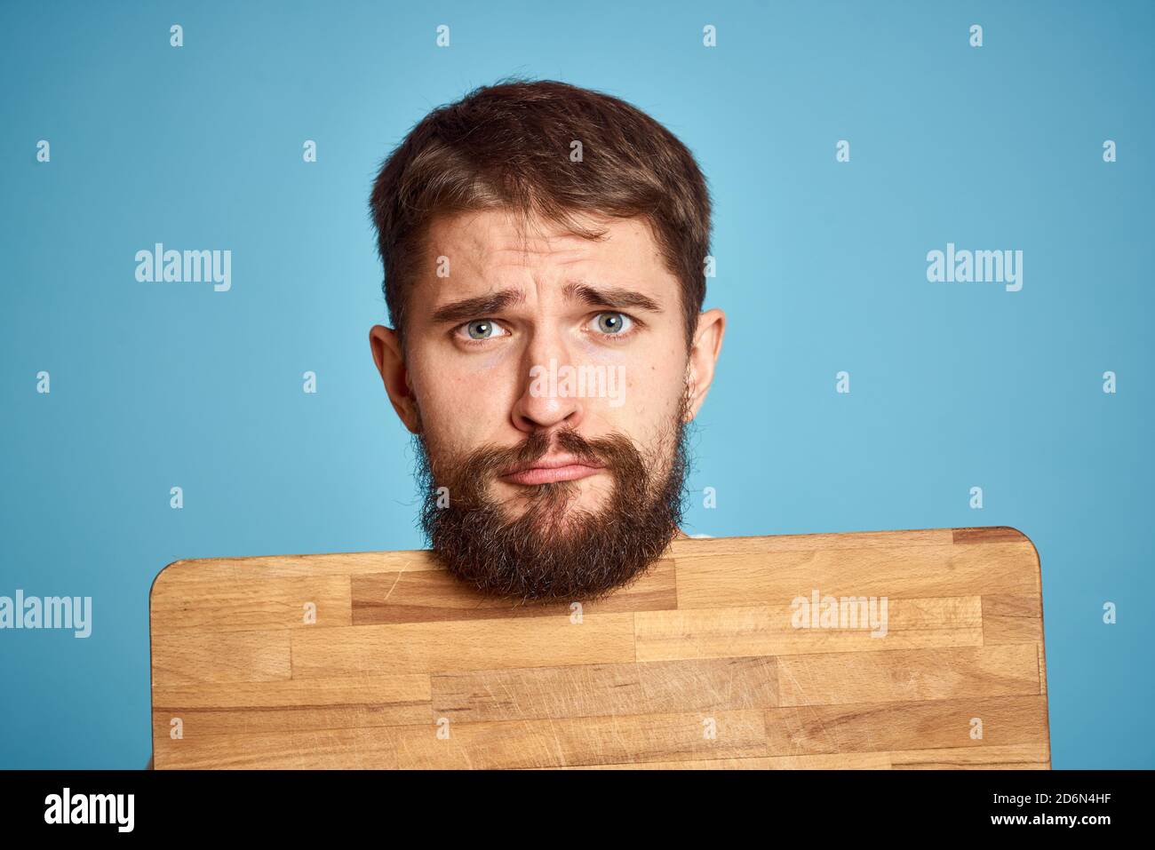 cute man with kitchen board near face on blue background emotions smile ...