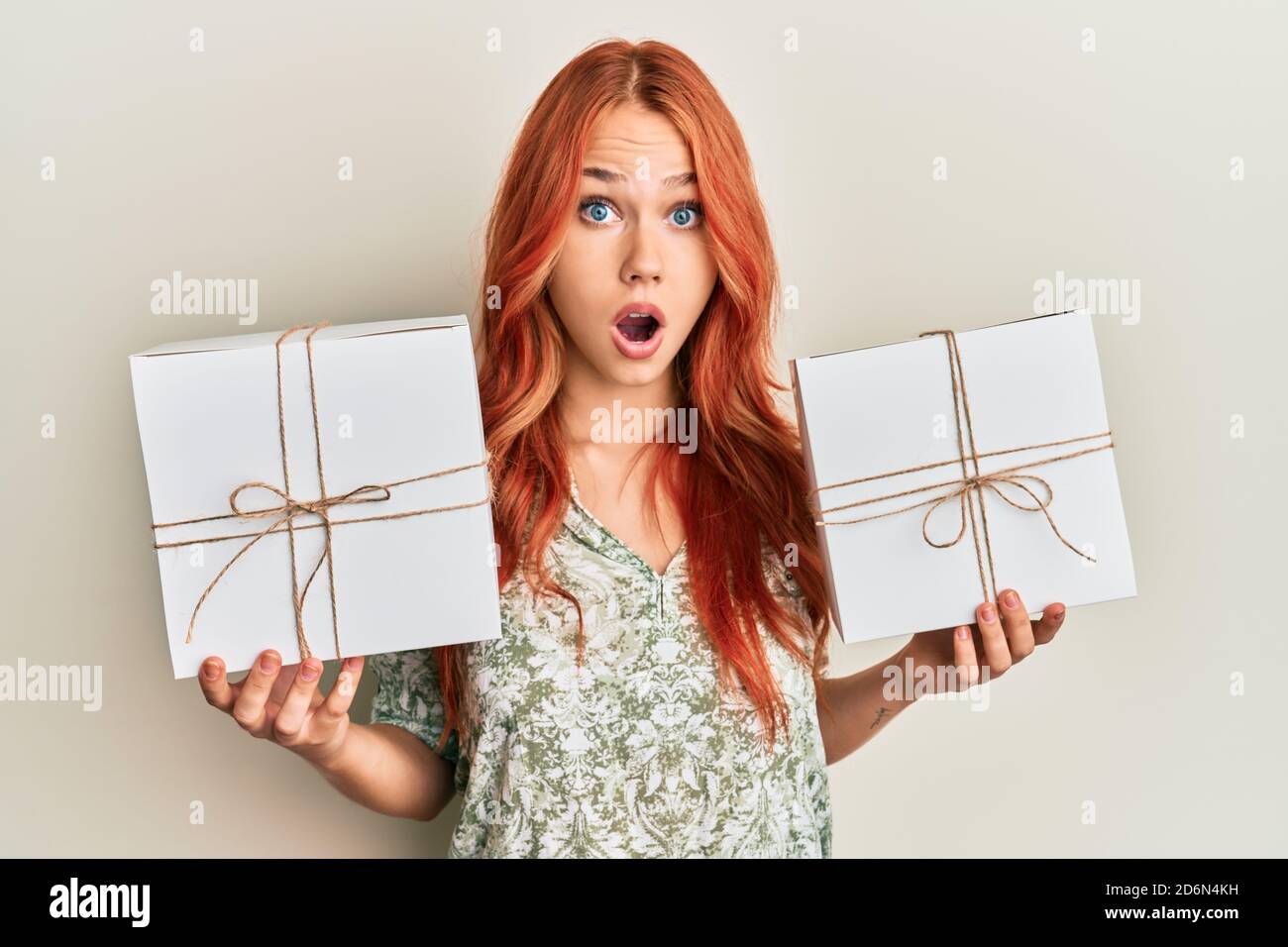 Young redhead woman holding gifts afraid and shocked with surprise and ...
